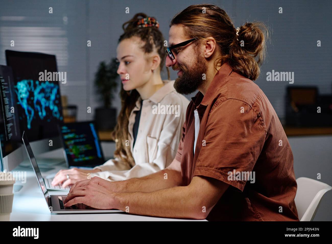Side view of young male IT engineer typing on laptop keyboard while decoding data on screen ...