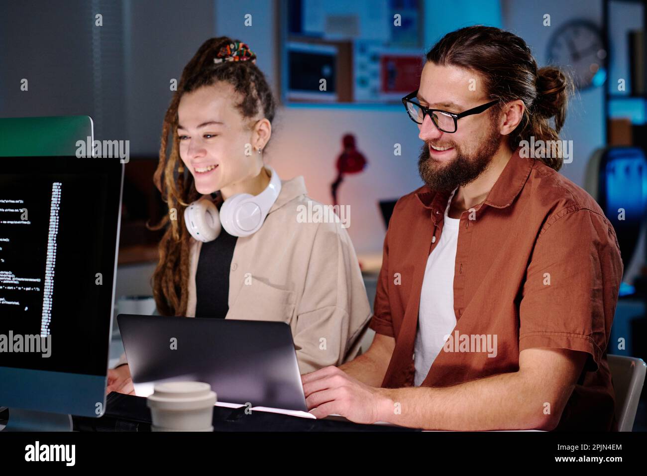 Two happy young IT managers sitting by workplace in front of computer ...