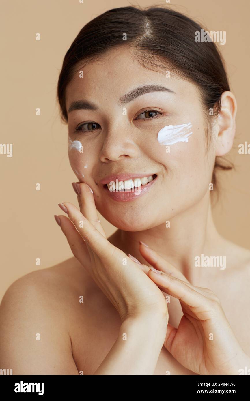 Portrait of modern woman with facial cream on face isolated on beige ...
