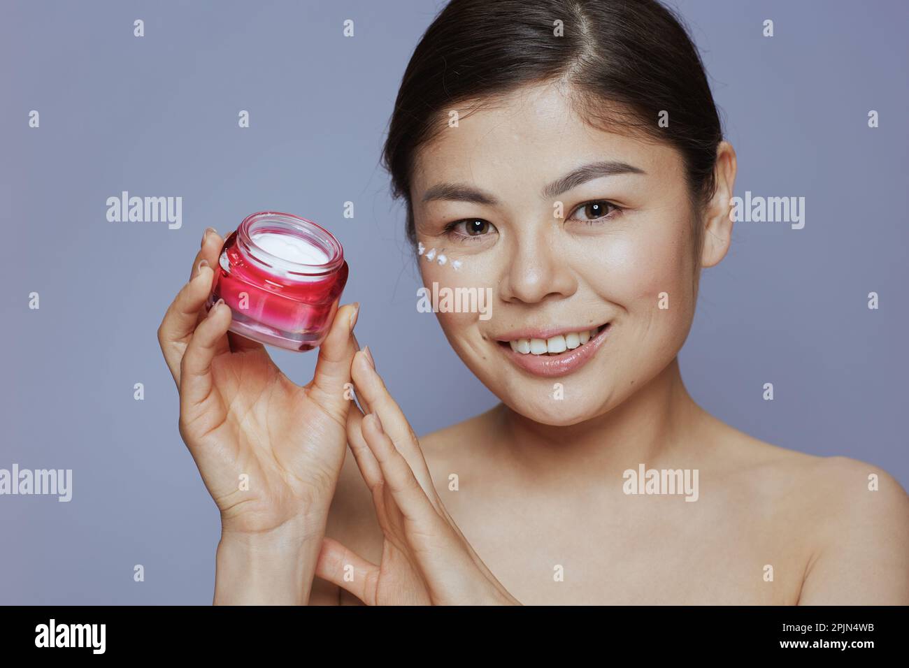 Portrait of modern asian female with facial cream jar and facial cream ...