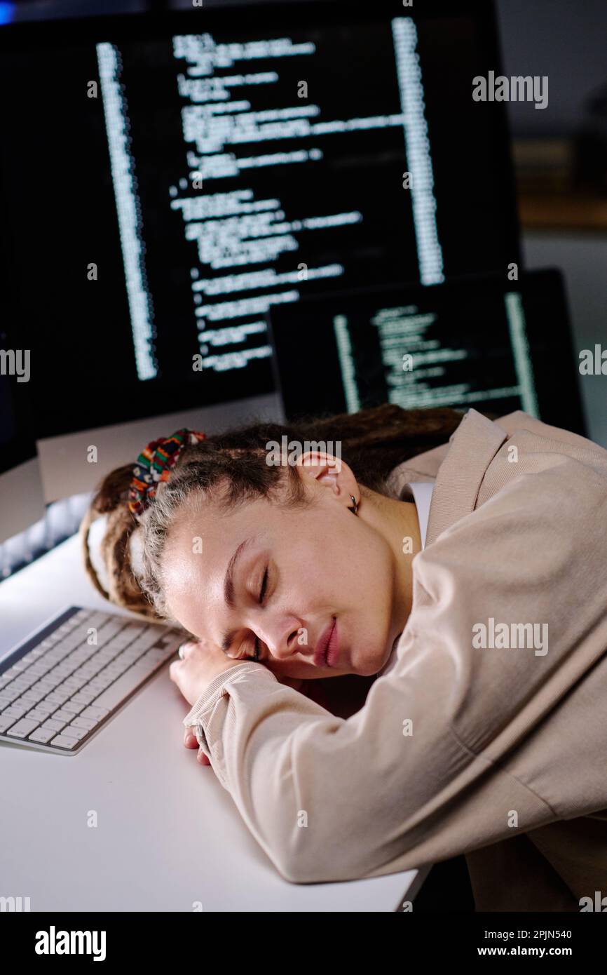 Young tired woman with dreadlocks keeping head on desk by keyboard ...