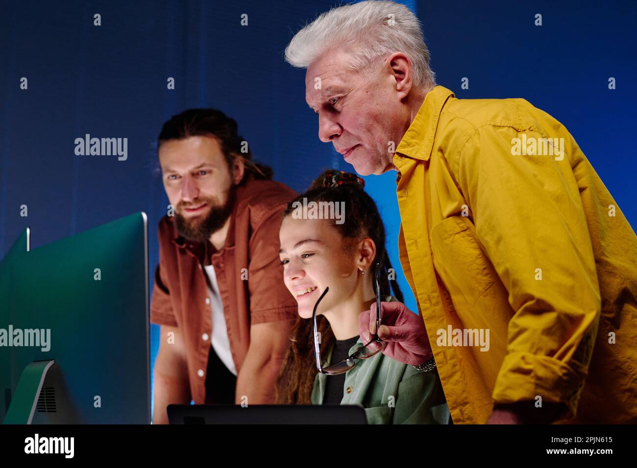 Team of programmers gathered in front of computer screen in dark office ...