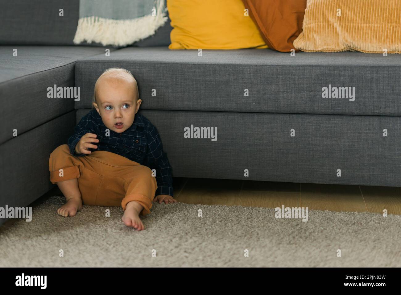 Frustrated scared toddler boy hiding behind a sofa copy space - concept ...