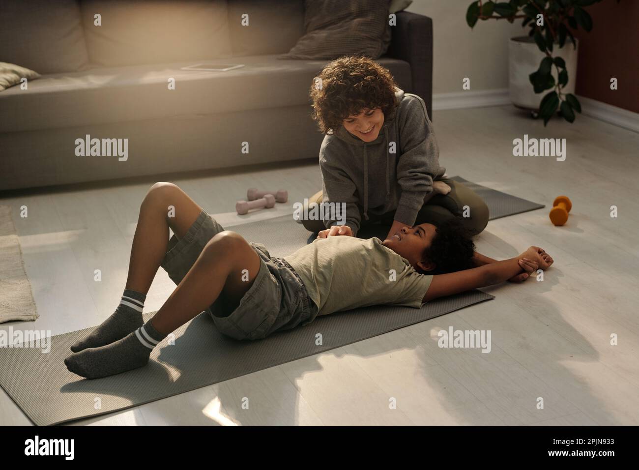Cute little boy lying on mat and chatting to his mother in activewear ...