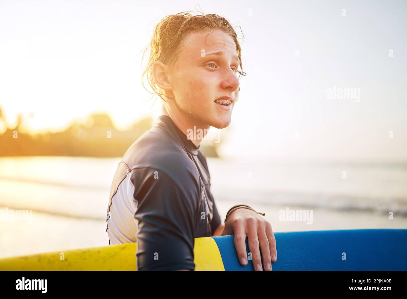 Portrait of a teen boy with Dental braces and wet hair with a surfboard ...