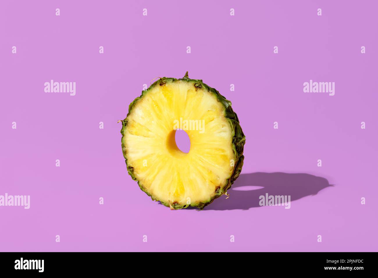 Single slice of pineapple in bright light minimalist on a purple table ...