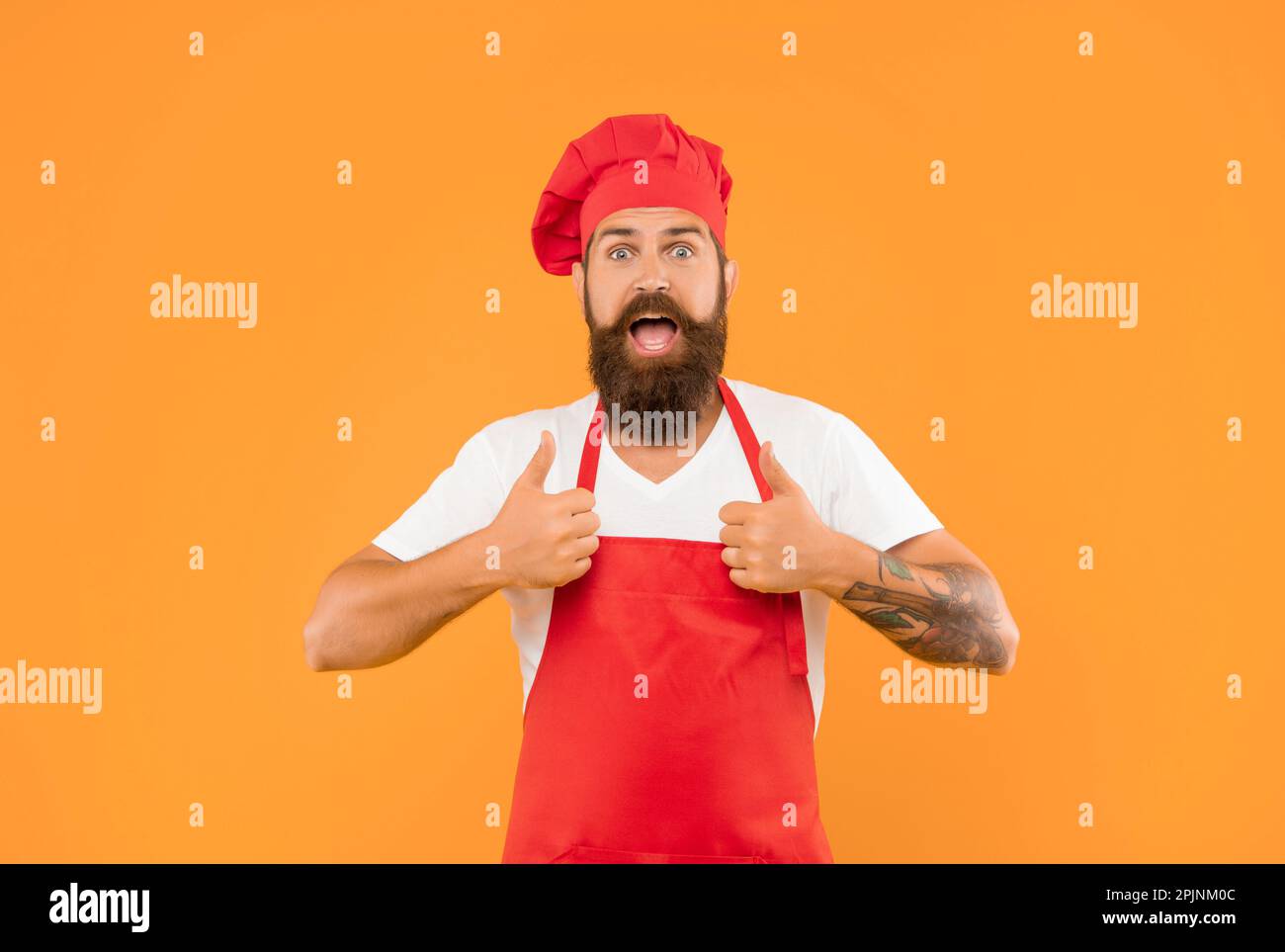 Surprised man in toque and apron giving double thumbs yellow background ...