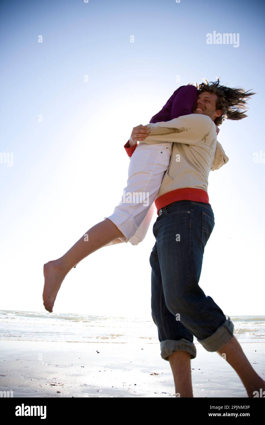 Young couple playing and messing around on a beach - man lifting woman ...