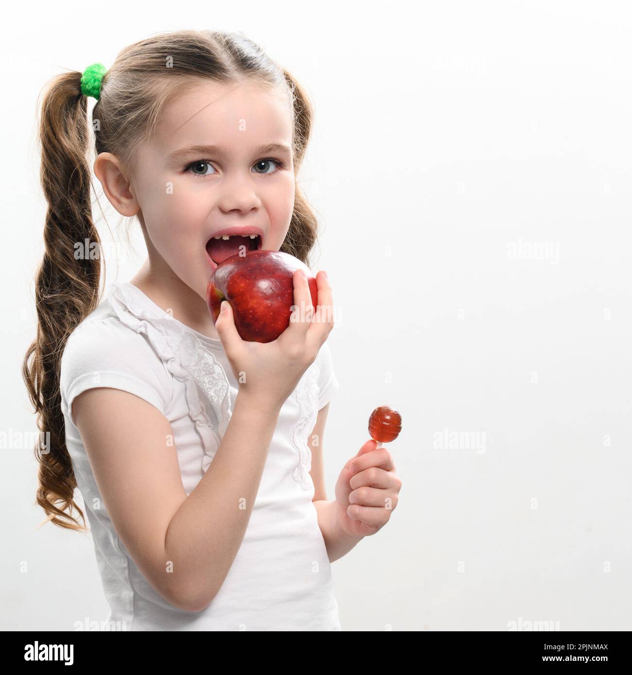 A child bites a big red apple and holds a lollipop in his hand on a ...