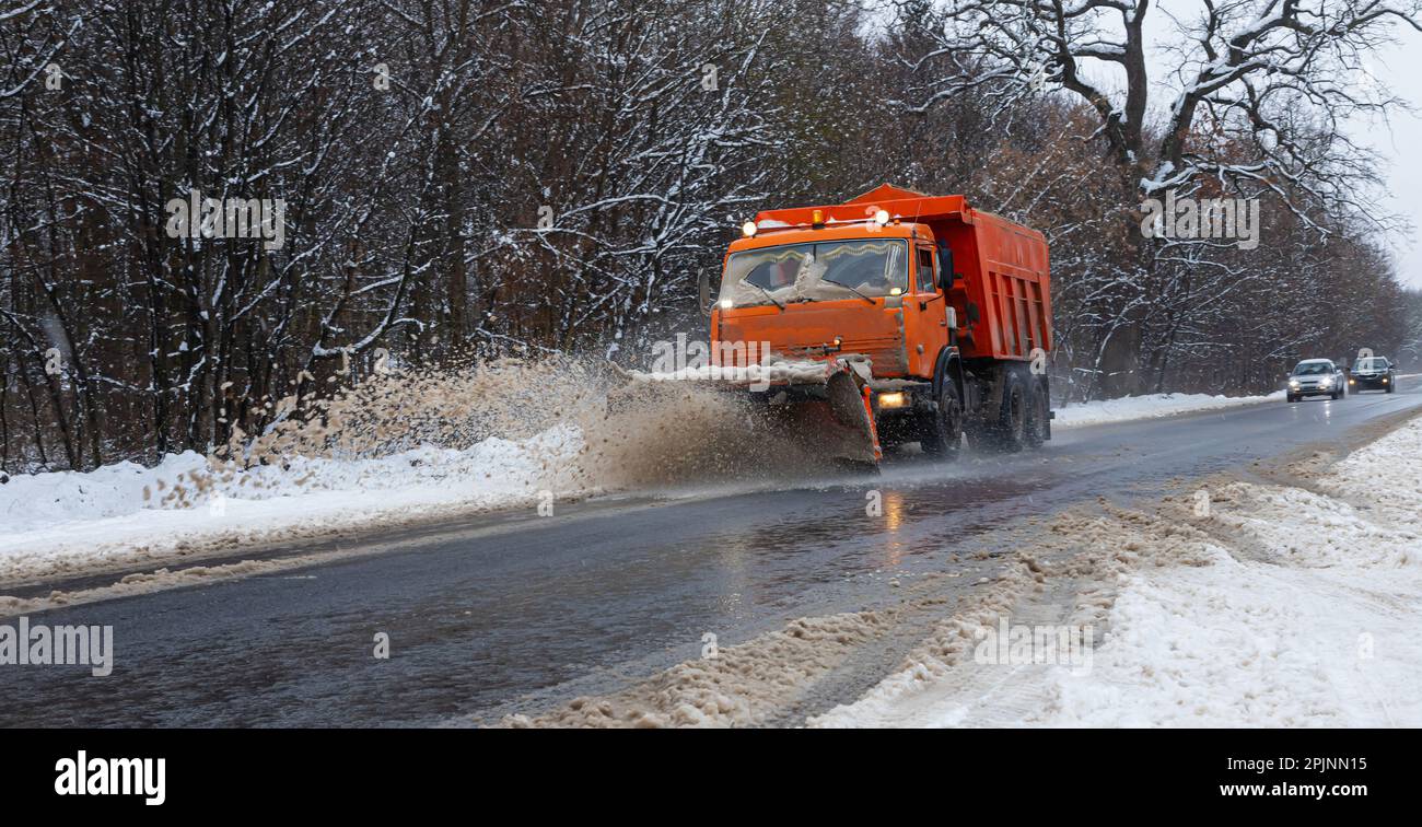 A large car with a plow clears the road from snow. Orange cargo special ...