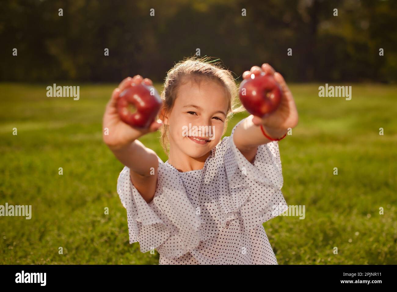 child girl holding red apples in hand and play in green park Stock ...