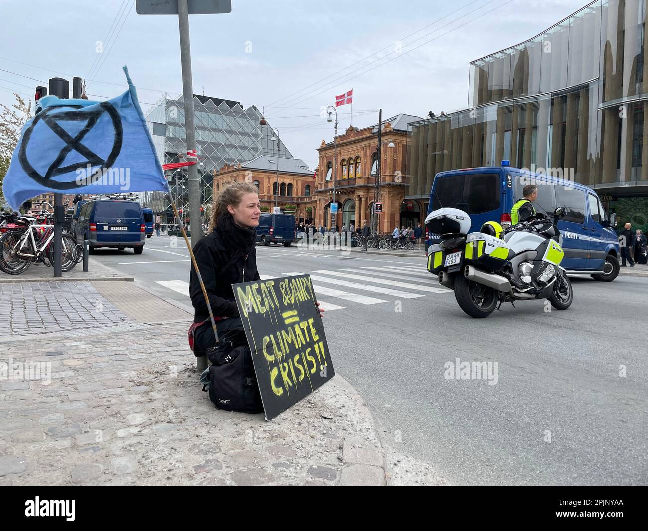 A female sitting on an urban sidewalk, holding an Extinction Rebellion ...