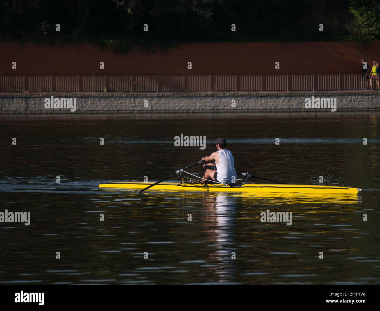 A man is paddling in a yellow kayak on a tranquil body of water Stock ...