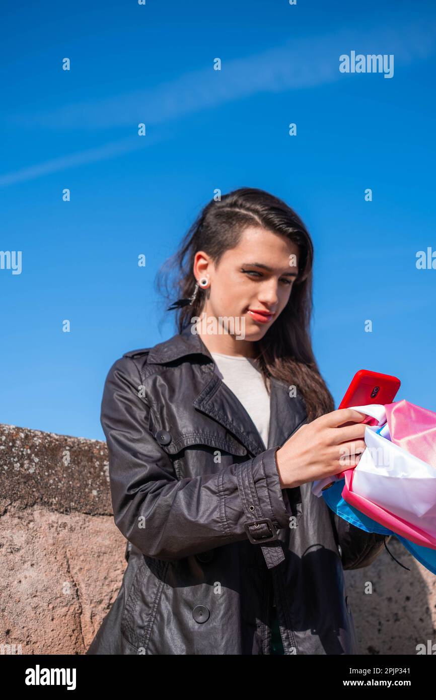 Transgender woman consulting her smartphone with the trans flag ...