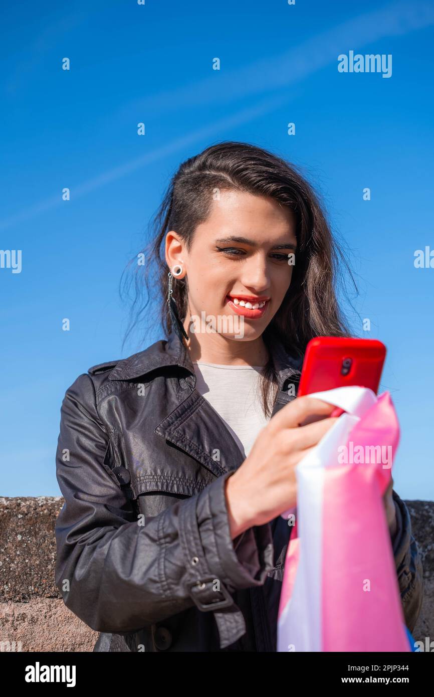 Transgender woman consulting her smartphone with the trans flag ...