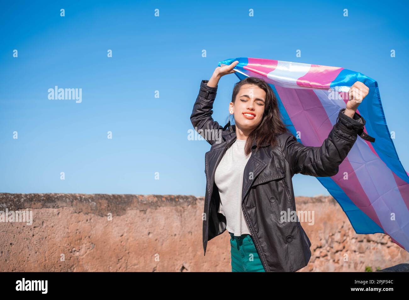Transgender woman raising the trans flag in flight with a clear sky in ...