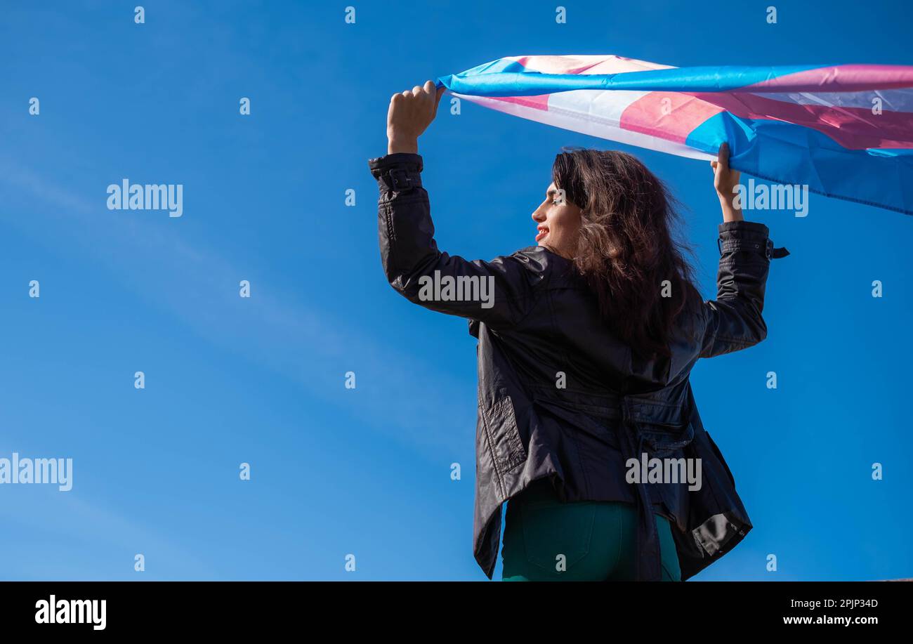 Transgender woman raising the trans flag in flight with a clear sky in ...