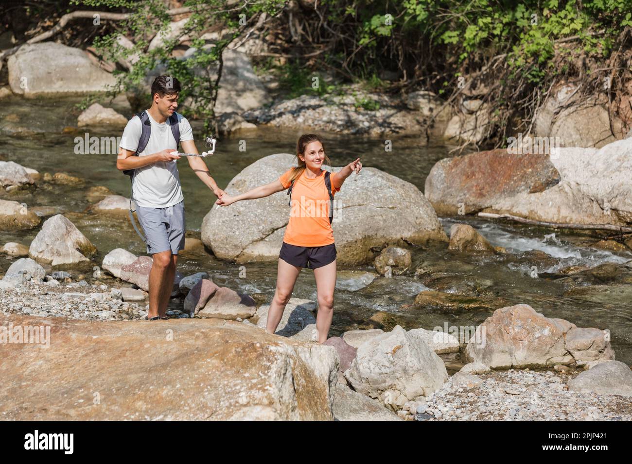 Active young hikers, man and woman walking over a mountain stream ...