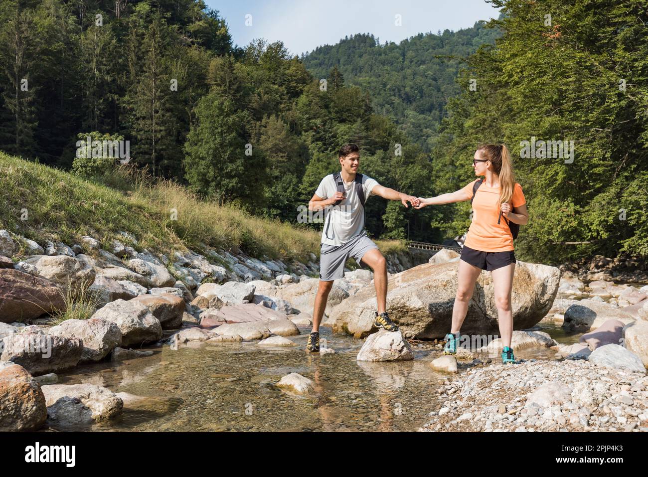 Active young hikers, man and woman walking over a mountain stream ...