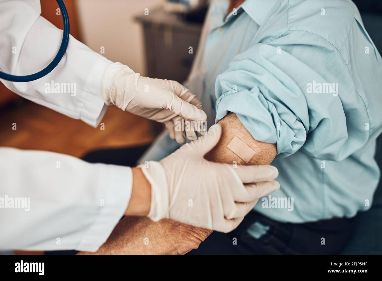Doctor putting a plaster in place of injection of vaccine to senior man ...
