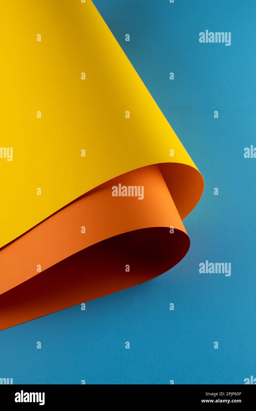 Close up of yellow and orange paper on blue background with copy space ...