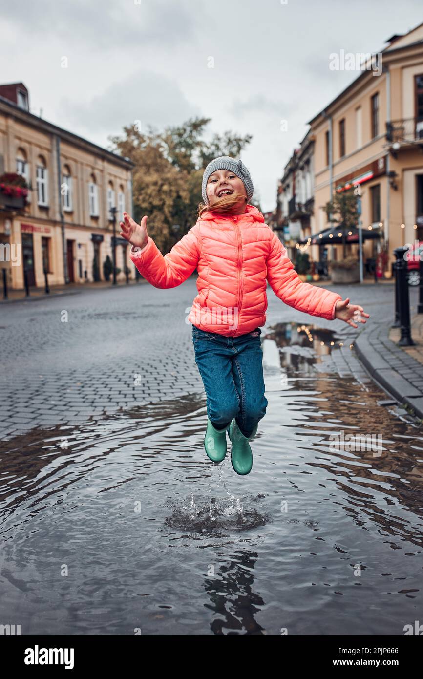 Happy smiling girl jumping in the puddle during walk in a downtown on ...