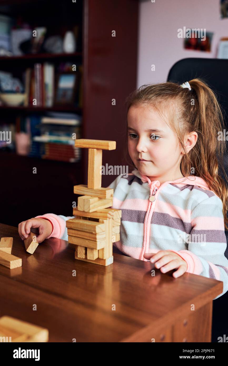 Little girl preschooler playing with wooden blocks toy building a tower ...