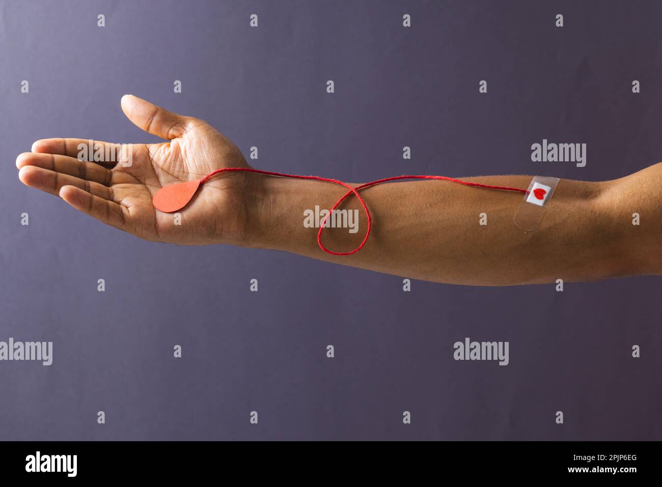 Arm of biracial man with heart sticking plaster and red string with ...