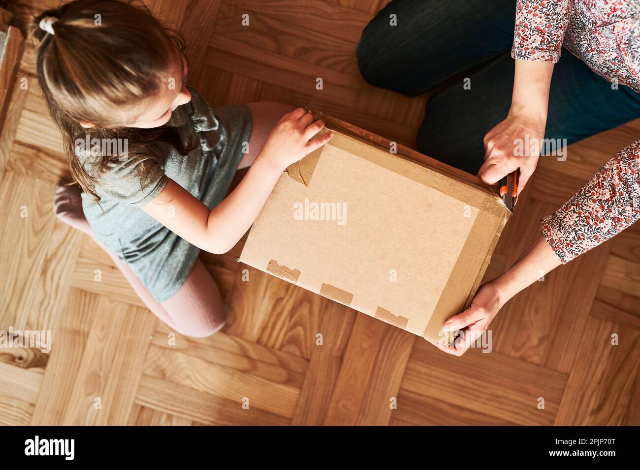 Woman unpacking a cardboard box parcel in room at home. Little girl ...