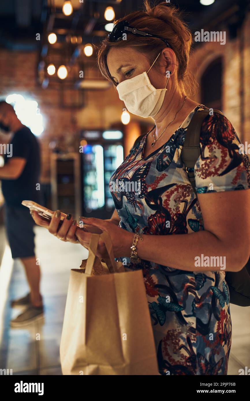 Young woman shopping in grocery store in the evening, wearing the face ...