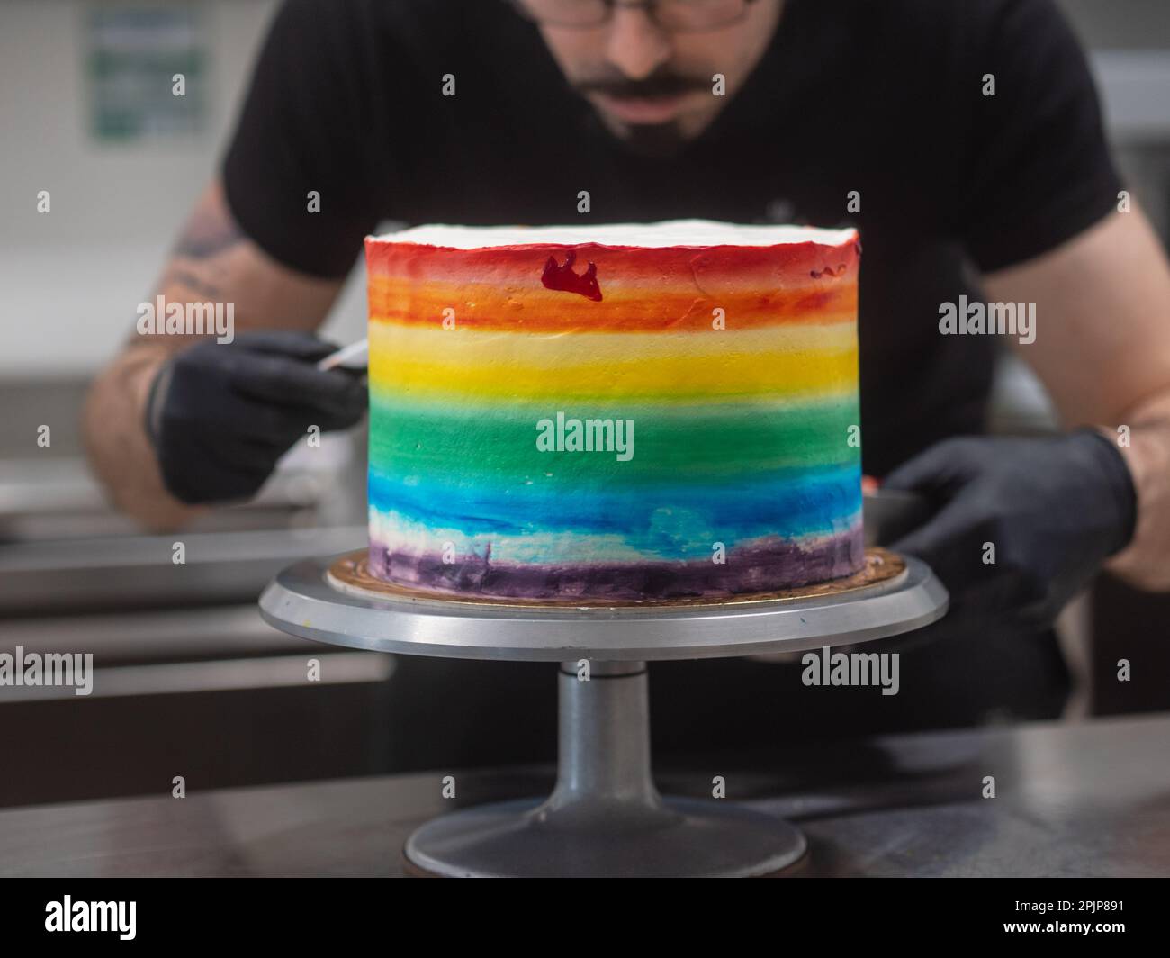 pastry chef working on a frosted cup cake with lgbt rainbow colours for ...