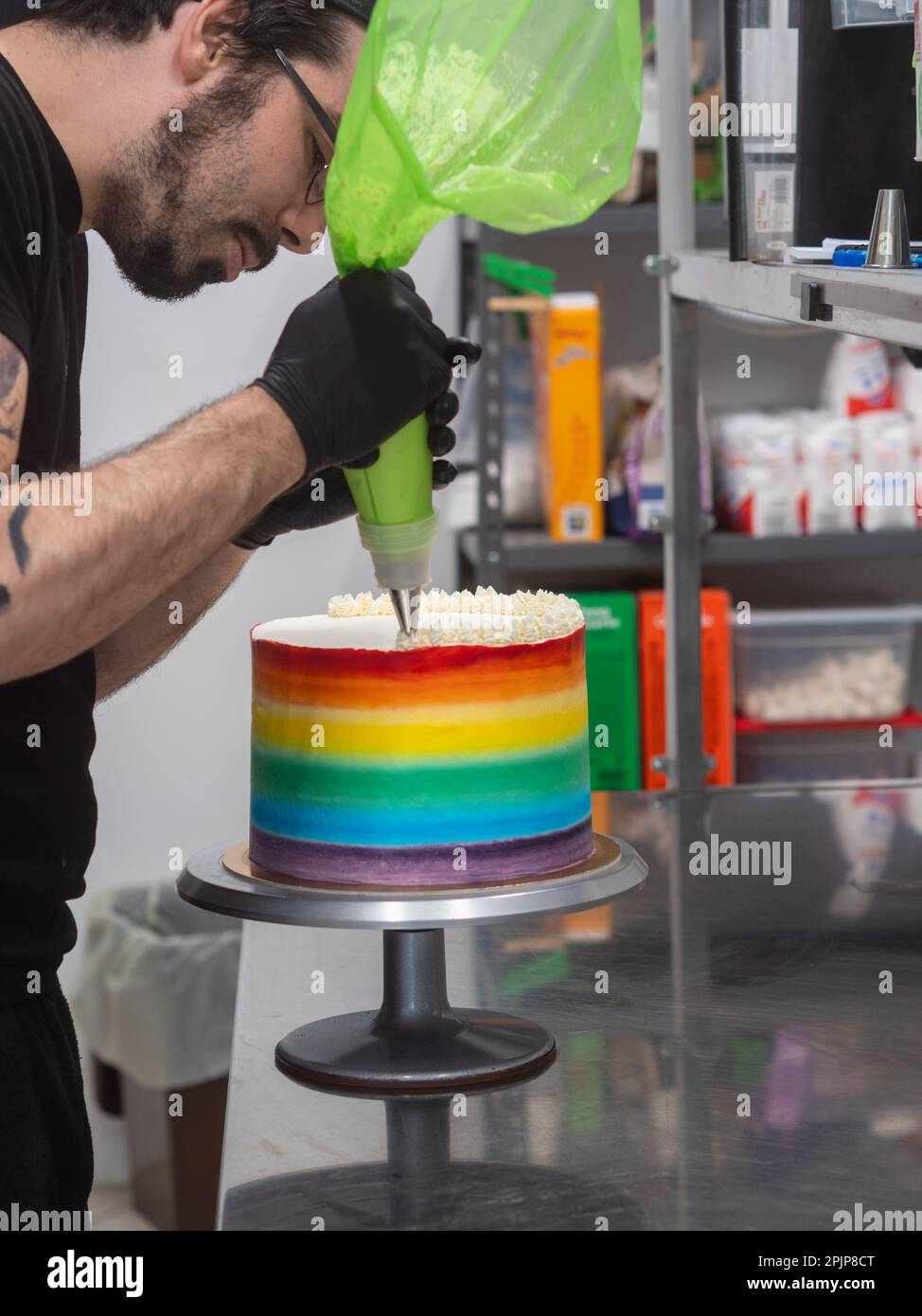 pastry chef working on a frosted cup cake with lgbt rainbow colours for ...