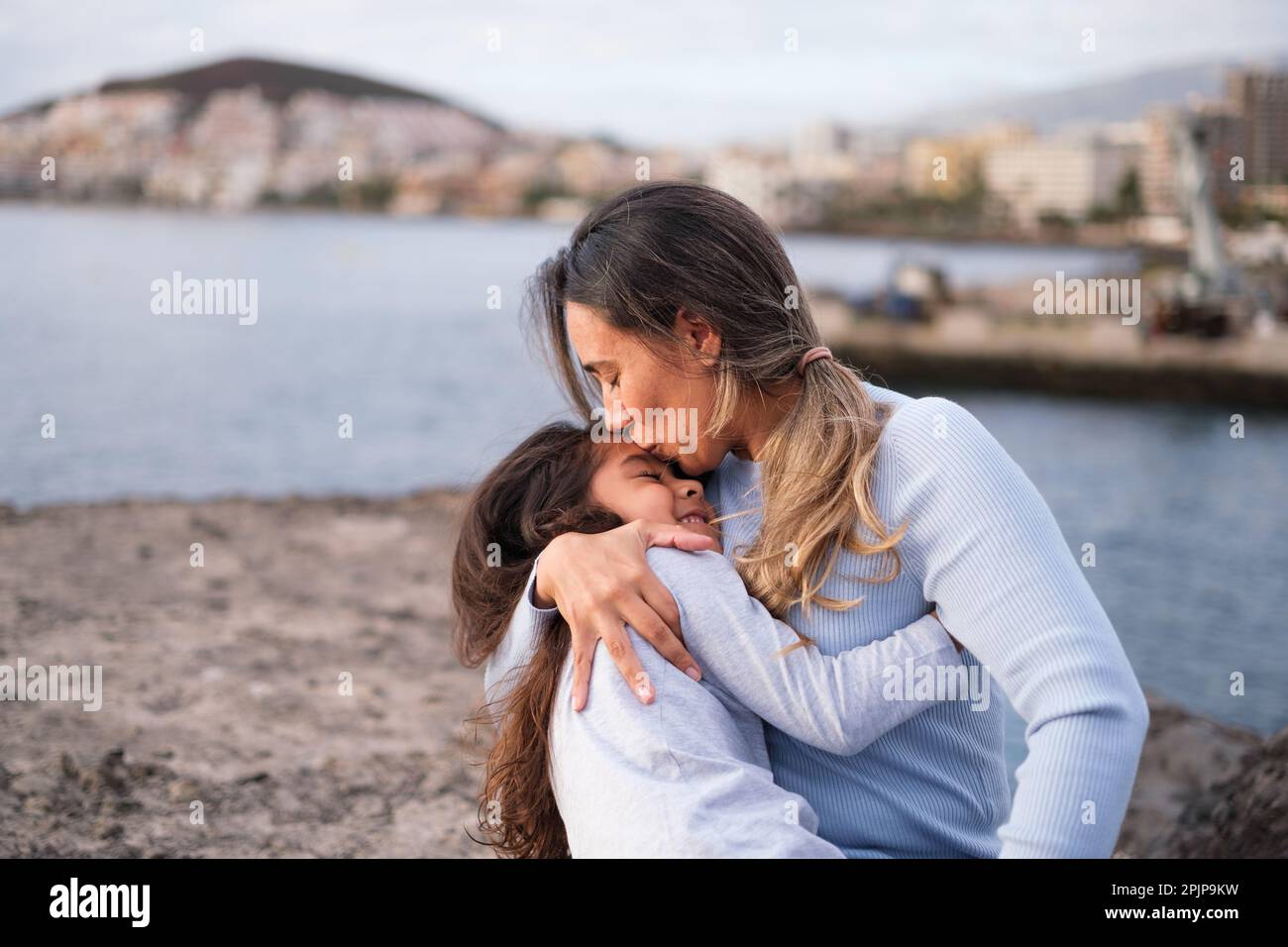 Mother hugging her little daughter on a walk by the sea and giving her daughter a lot of love ...