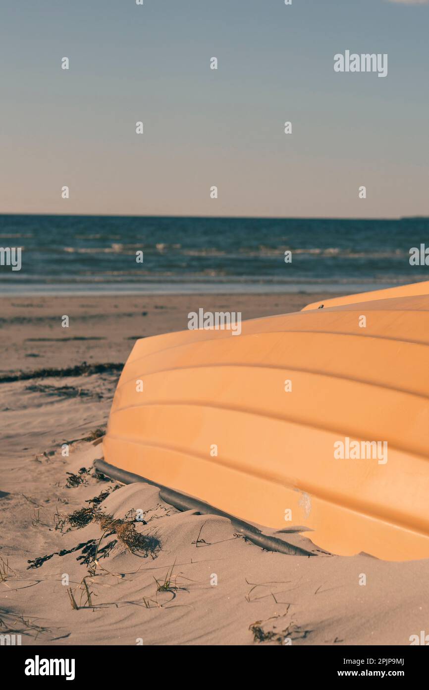 An orange sailing boat is pictured on a sandy beach in a coastal area ...