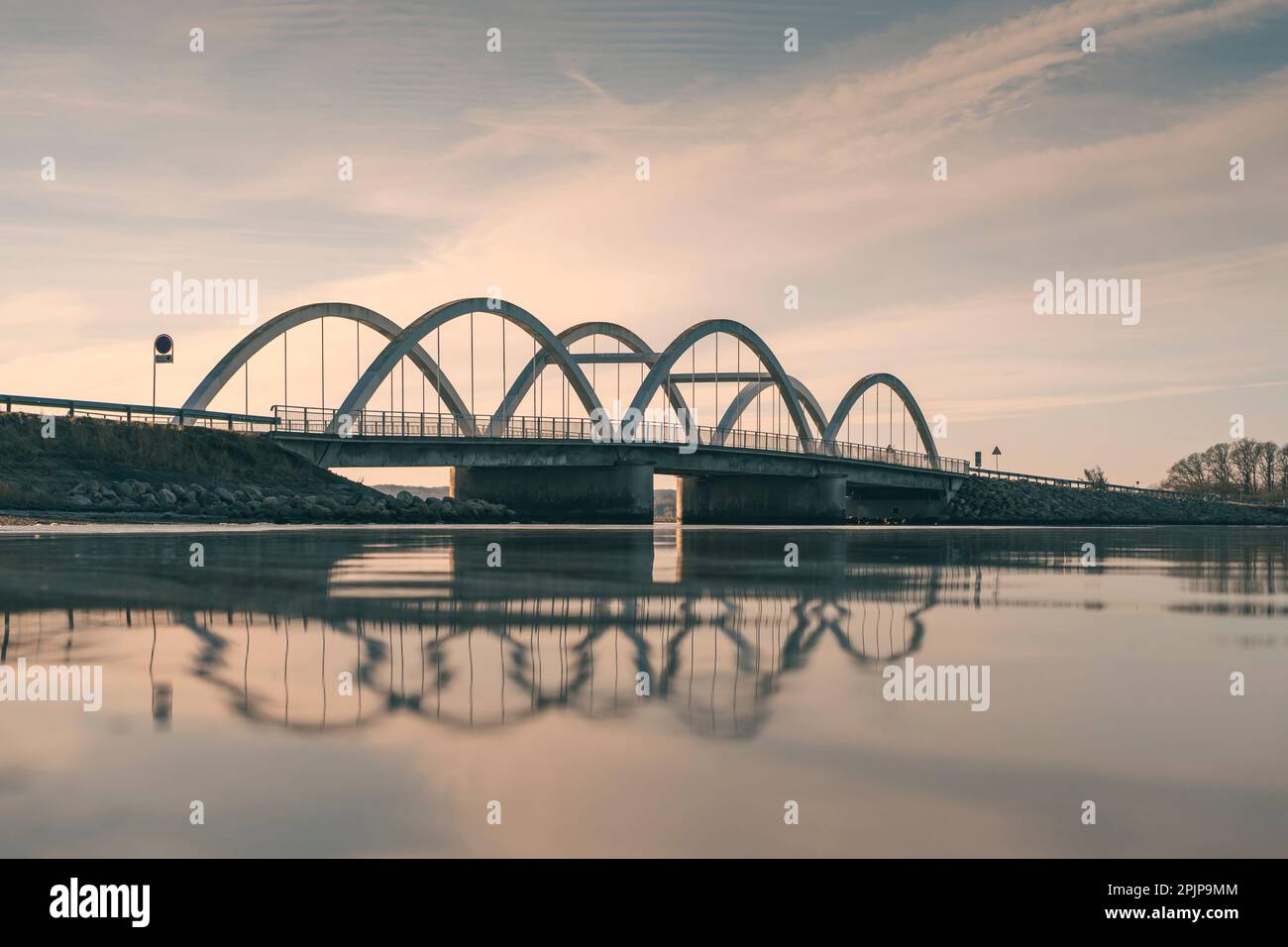 A picturesque arched bridge spanning a tranquil body of water at sunset ...