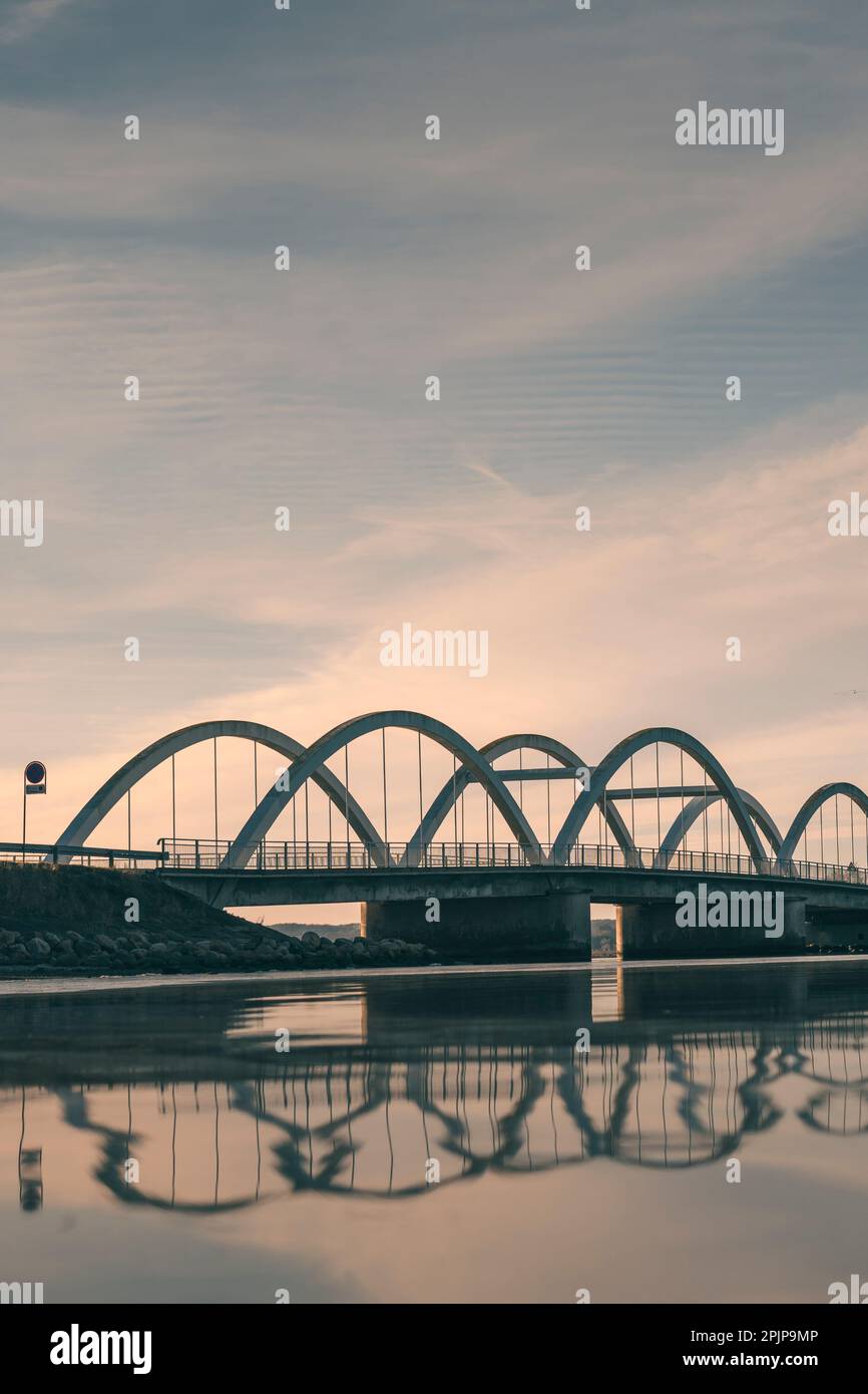 A picturesque arched bridge spanning a tranquil body of water at sunset ...