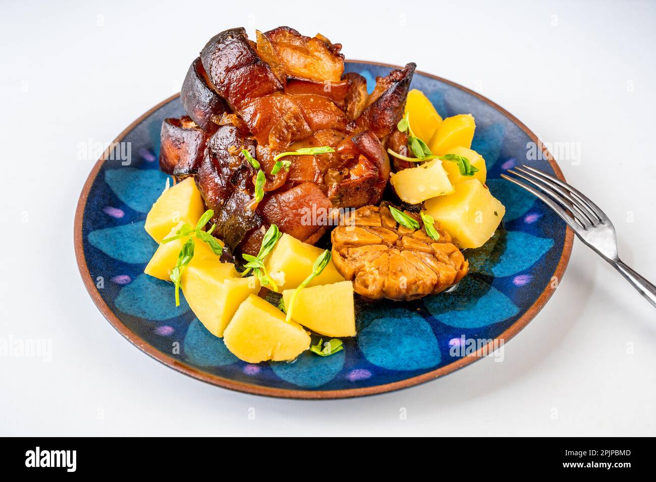 Baked spicy pork belly, garlic and boiled potato on decorative blue ...
