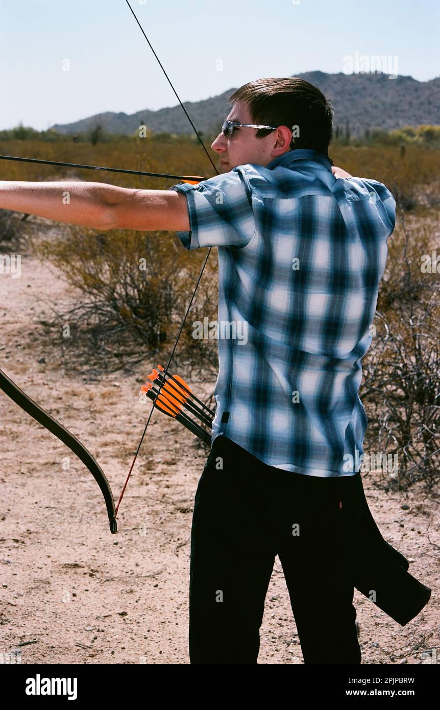 Young man shooting a bow and arrow in the desert Stock Photo - Alamy