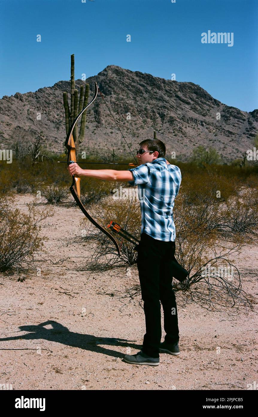 Young man shooting a bow and arrow in the desert Stock Photo - Alamy
