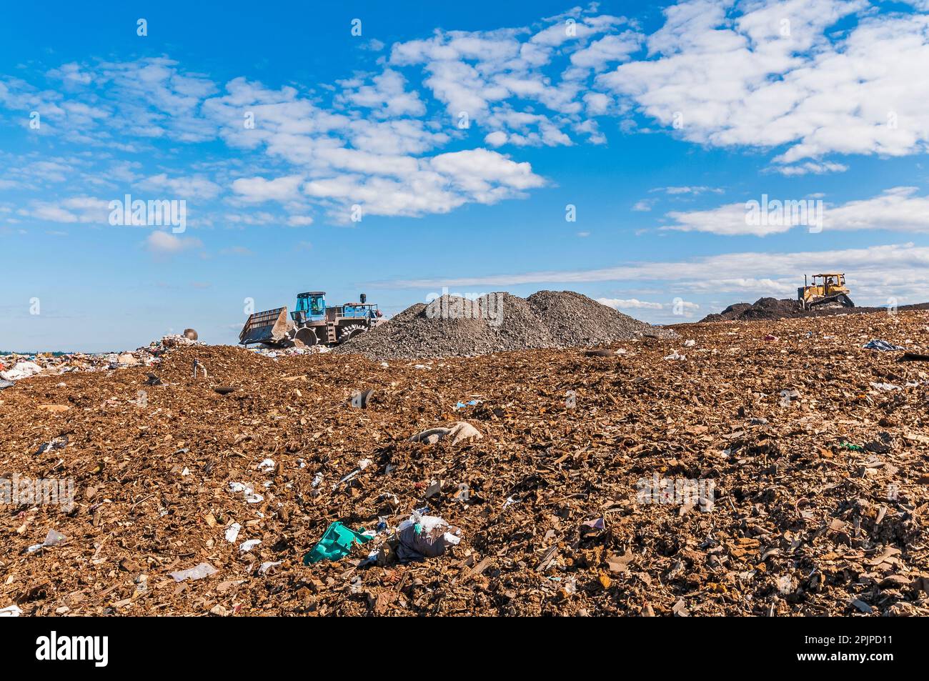 A soil compactor and a bulldozer work the land in an active landfill ...