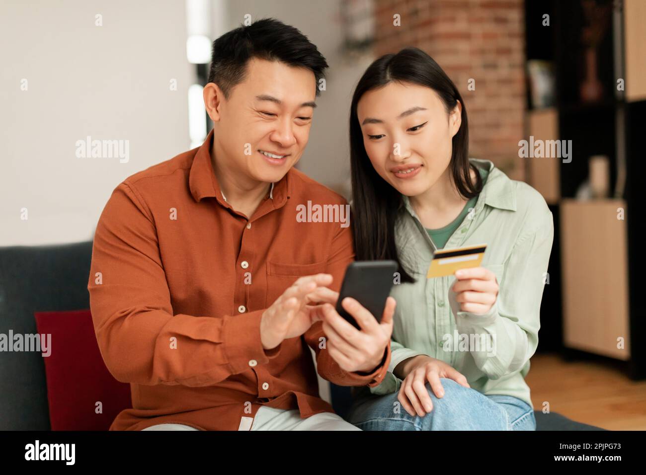 Family shopping online. Korean husband and wife using cellphone and credit card, making payment ...