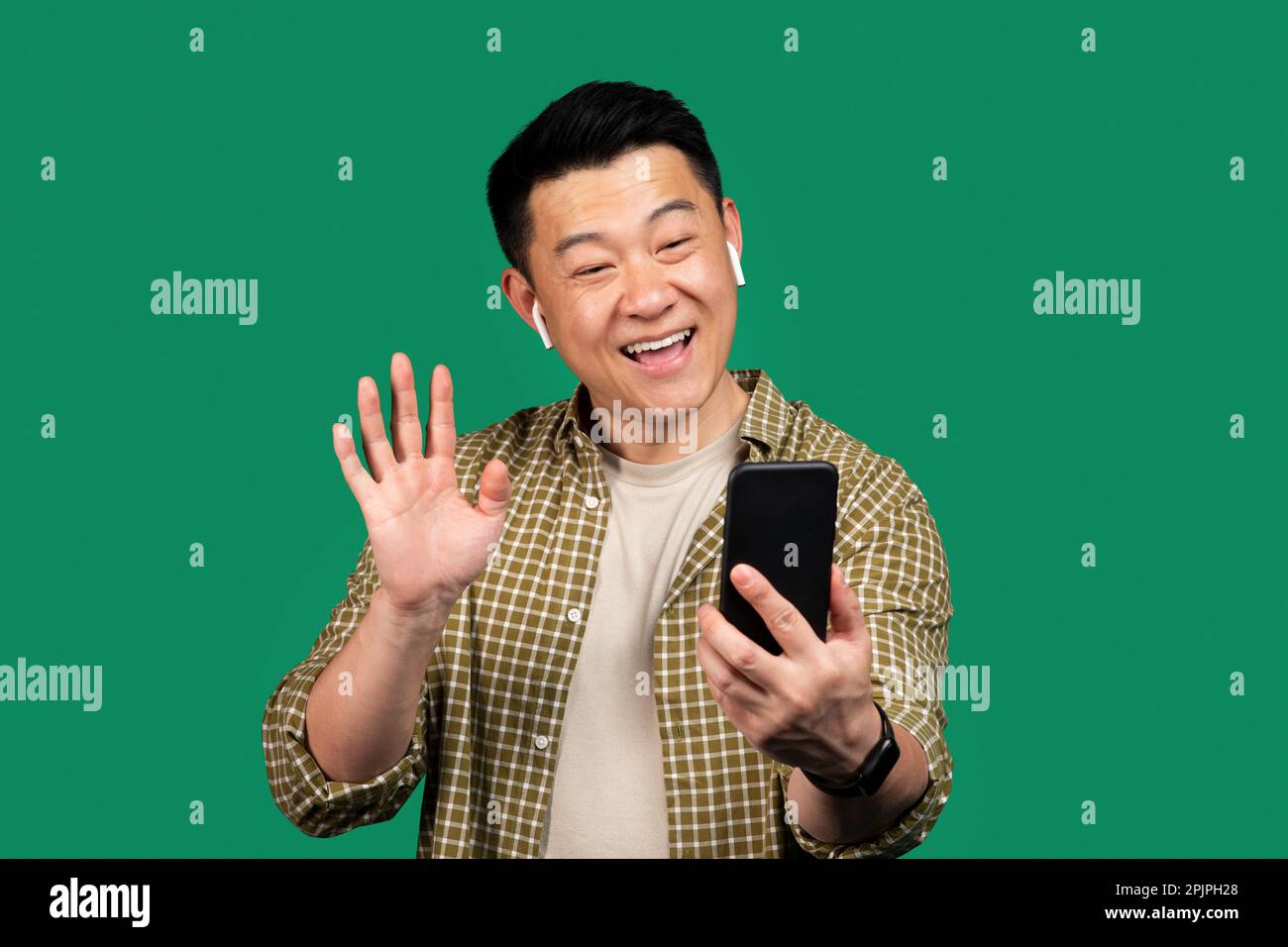 Positive korean man making video call via cellphone, wearing earphones ...