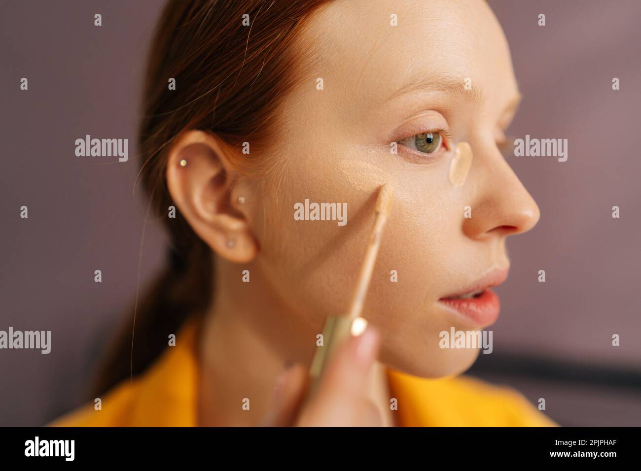 Close-up face of pretty young woman applying concealer on face under ...