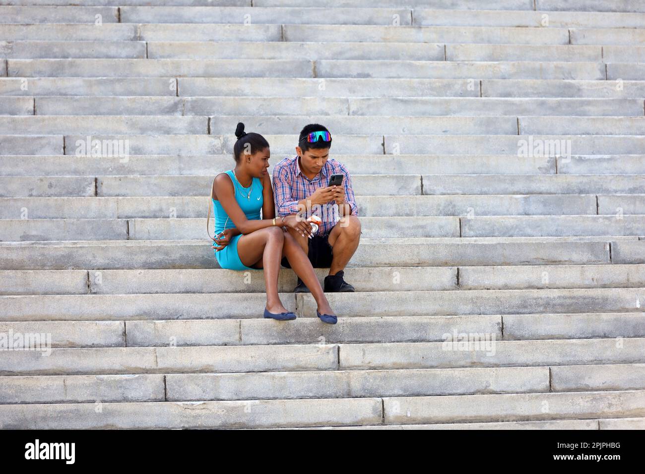 Cuban couple sitting with smartphone on stone steps of National Capitol ...