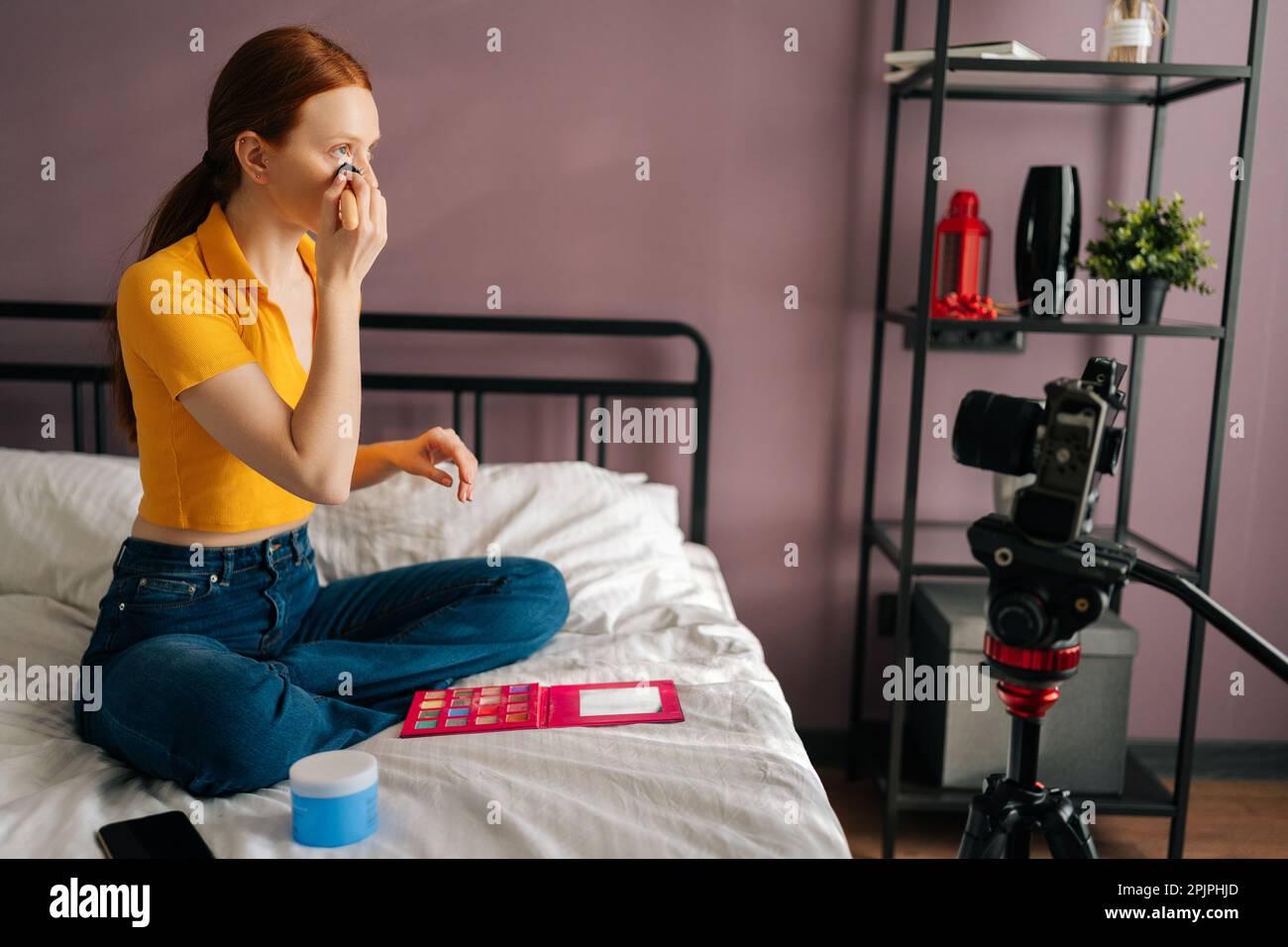 Side view of red-haired young woman recording cosmetics product review ...