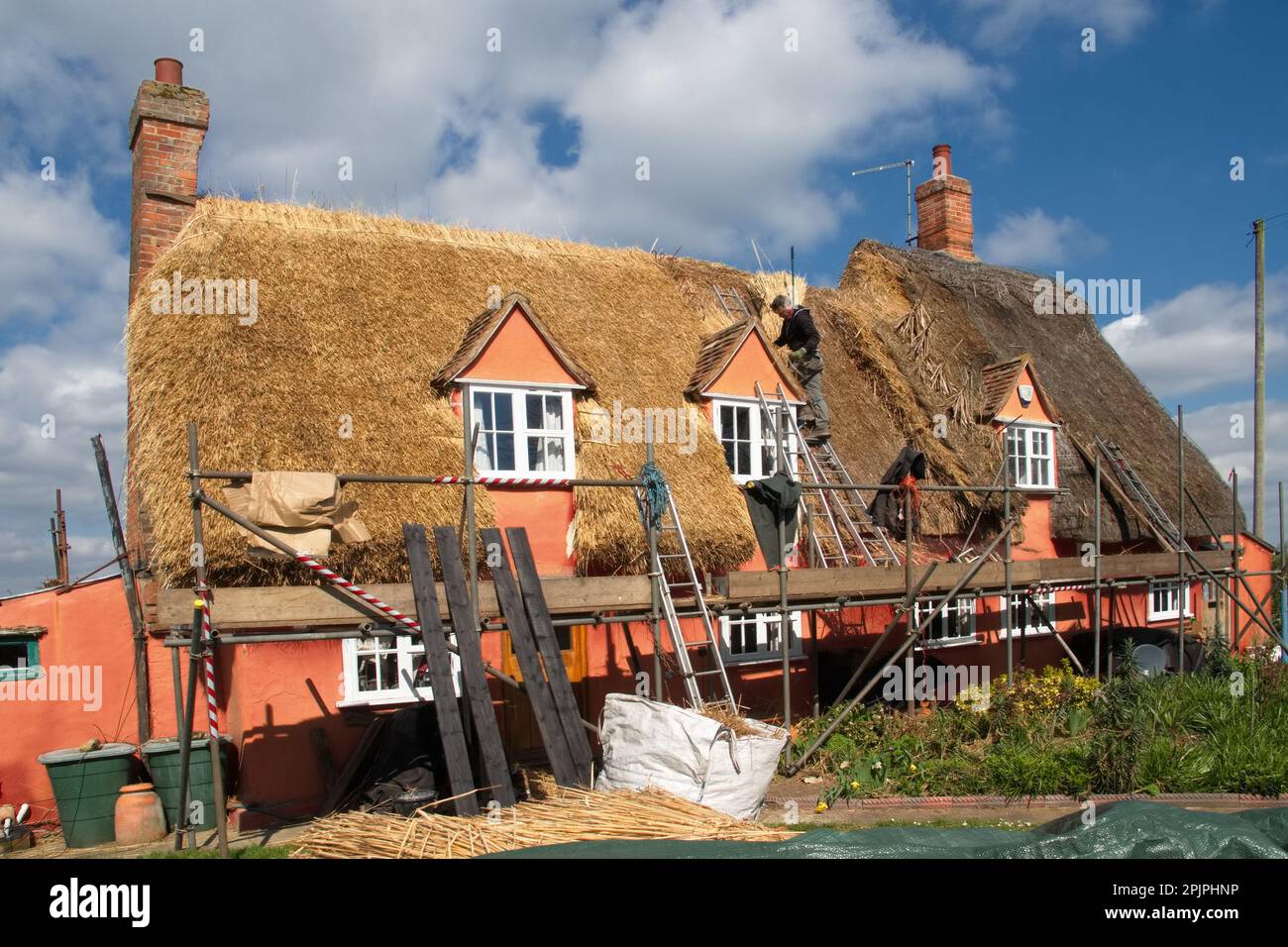 The picture shows a man working on the roof of an old English thatched ...