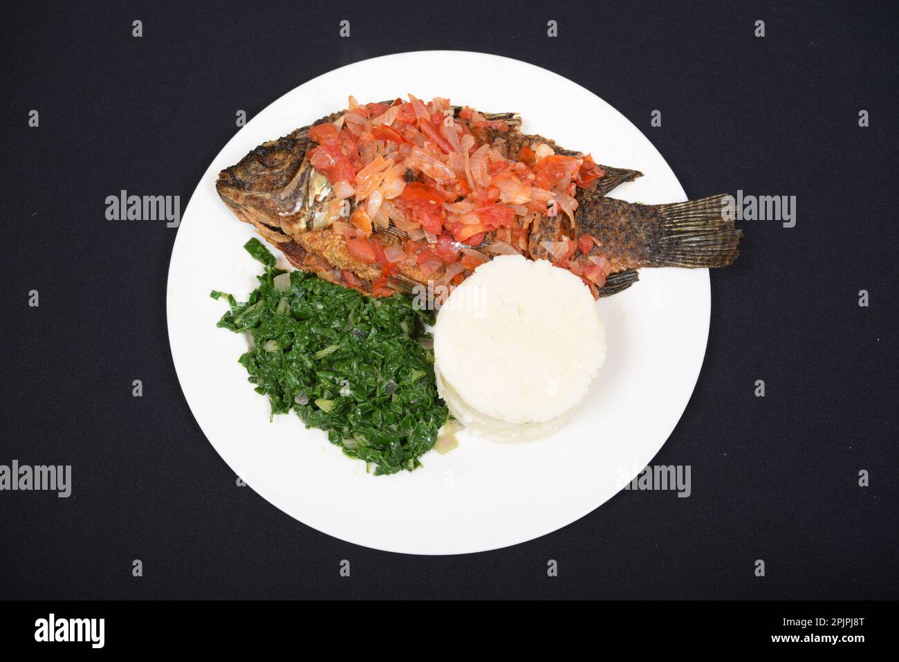 Grilled fish served with ugali and vegetables on an isolated background ...