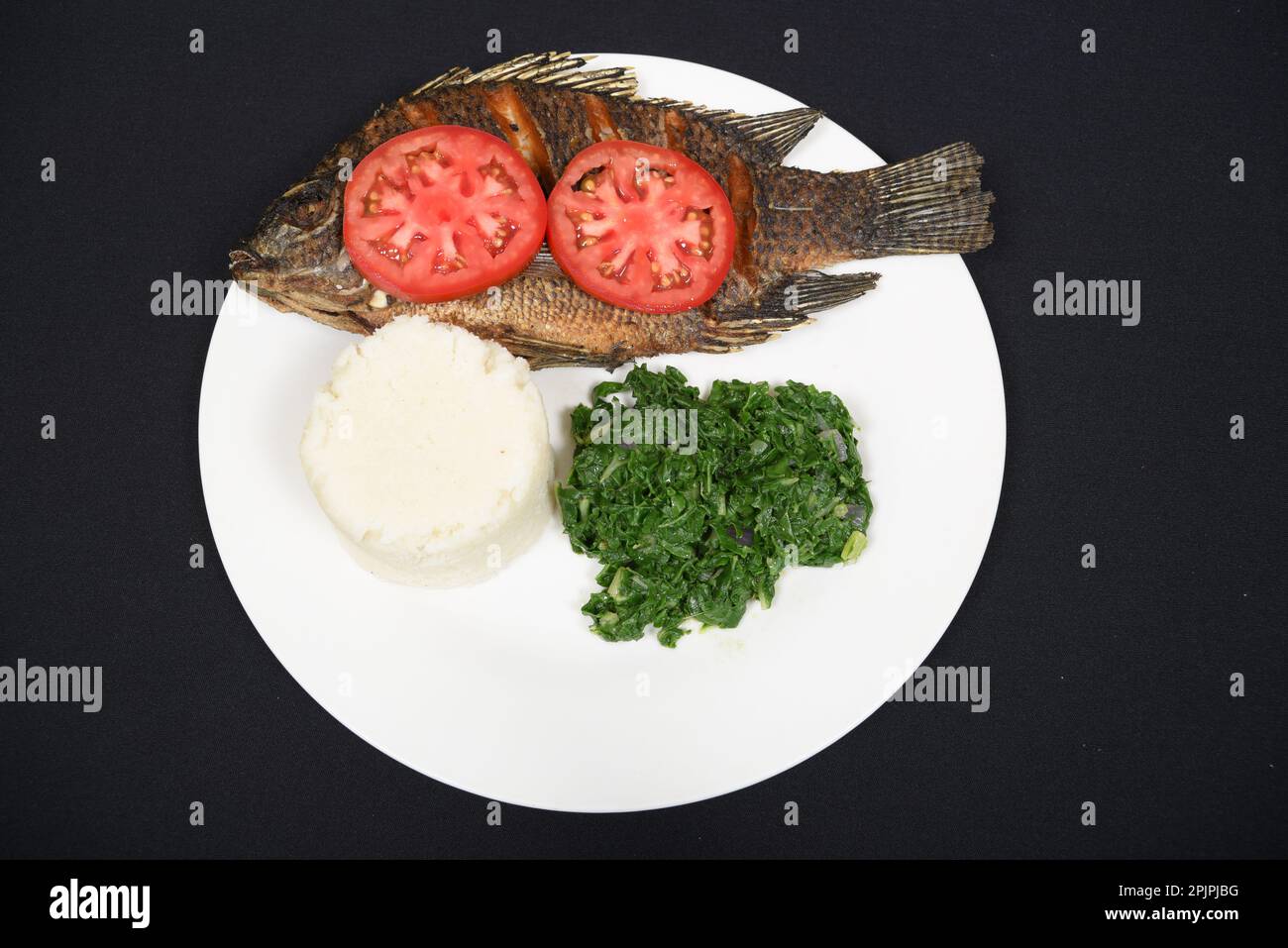 Grilled fish served with ugali and vegetables on an isolated background ...