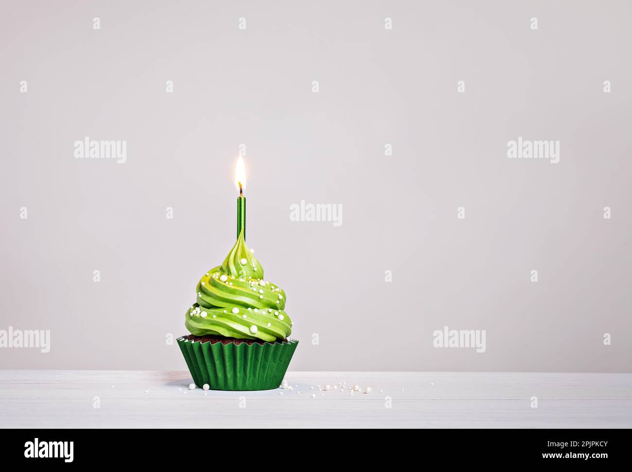 Green birthday cupcake with buttercream icing, sprinkles and lit candle on a light grey white ...