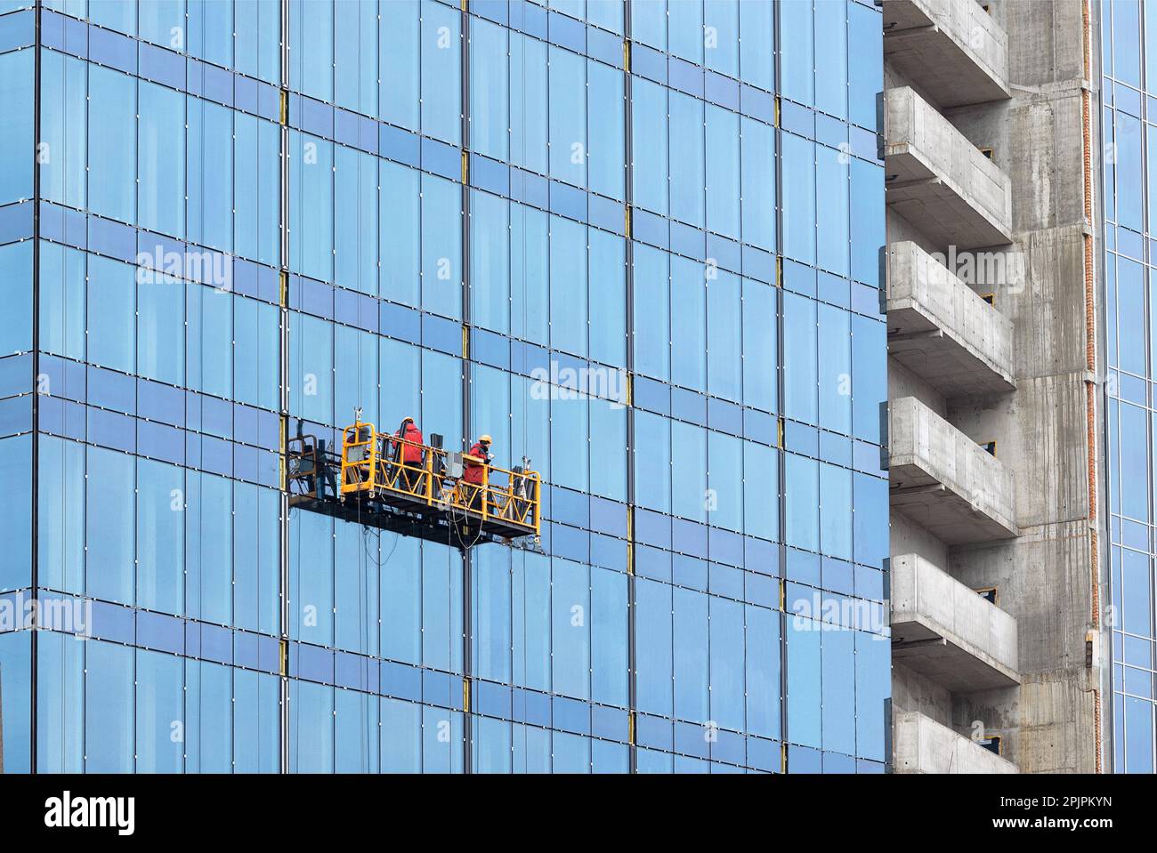 Construction workers on a suspended cradle mount the glass facade of a ...